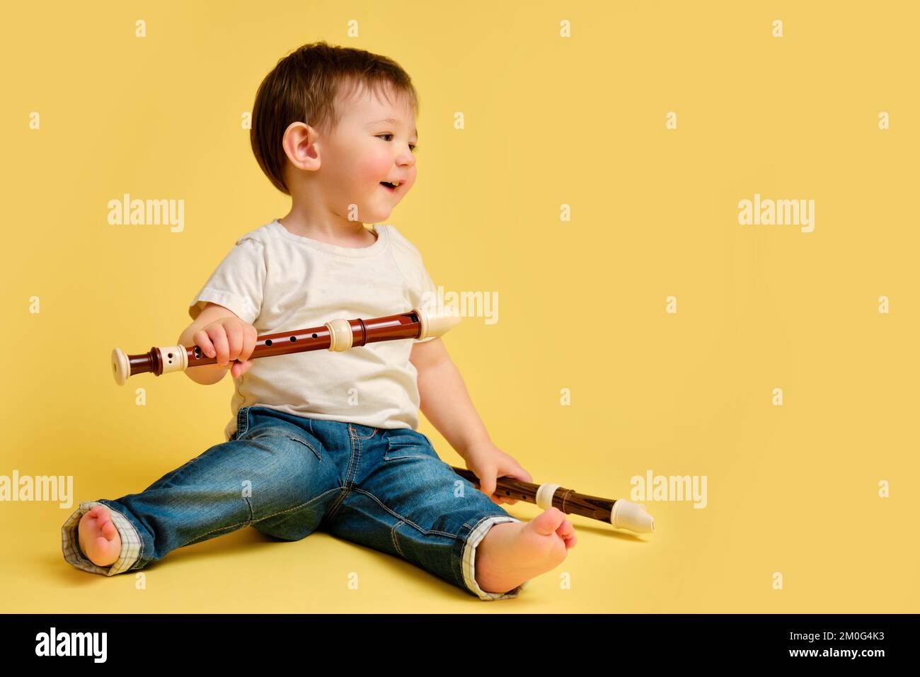 Toddler baby with a flute wind musical instrument on a studio yellow ...