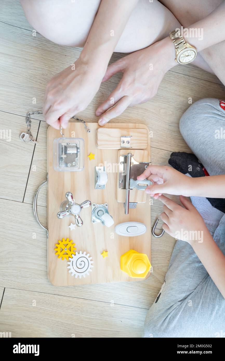 Child and mother are playing with busy board toy on the wooden floor ...