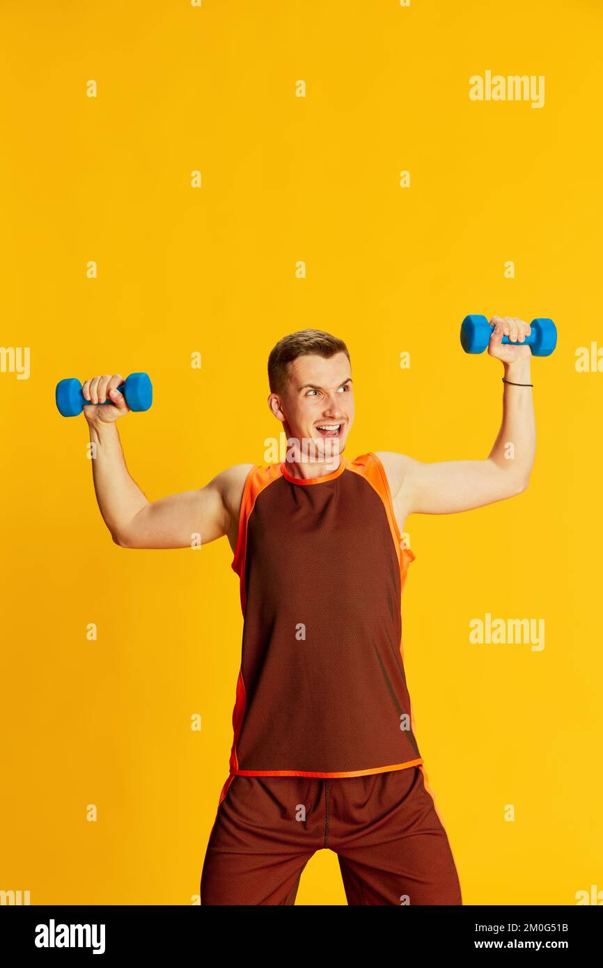Portrait of young man in orange uniform training, lifting dumbbells ...