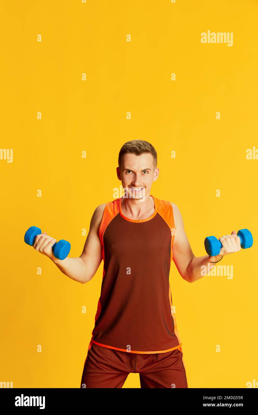Portrait of young man in orange uniform training with weights, posing ...