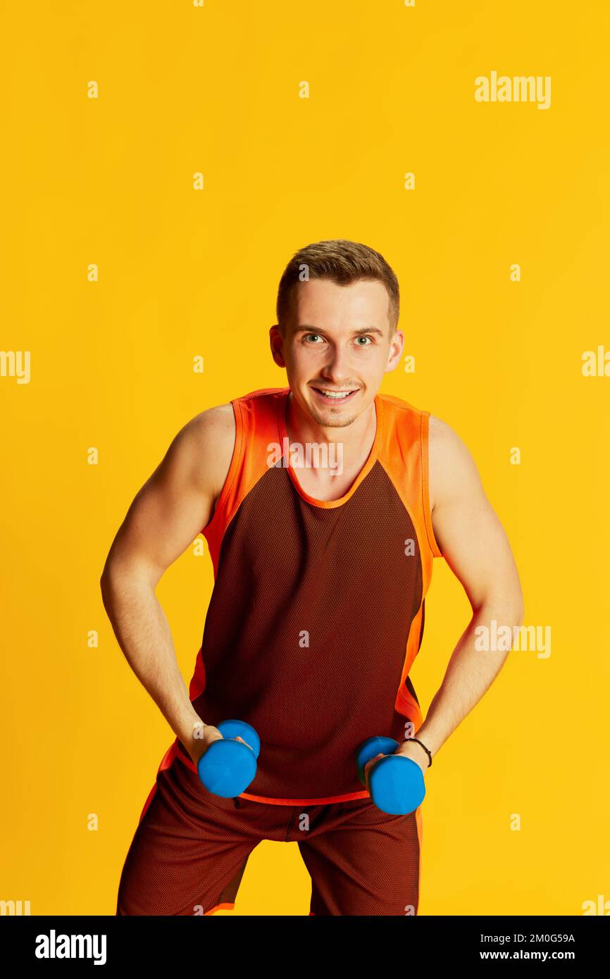 Portrait of young man in orange uniform training, posing with sports ...