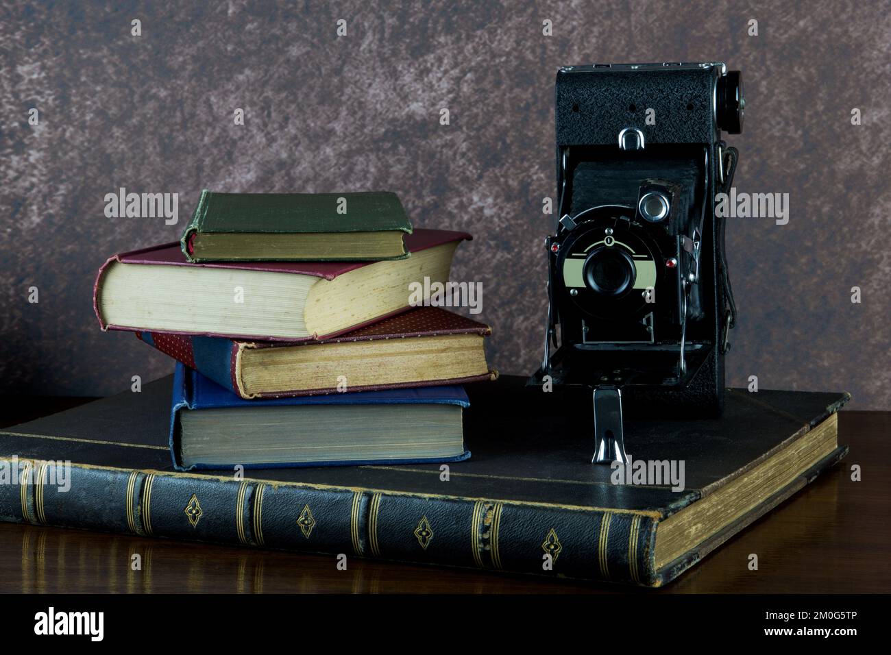 Old folding camera and pile of old books on a polished wooden surface ...