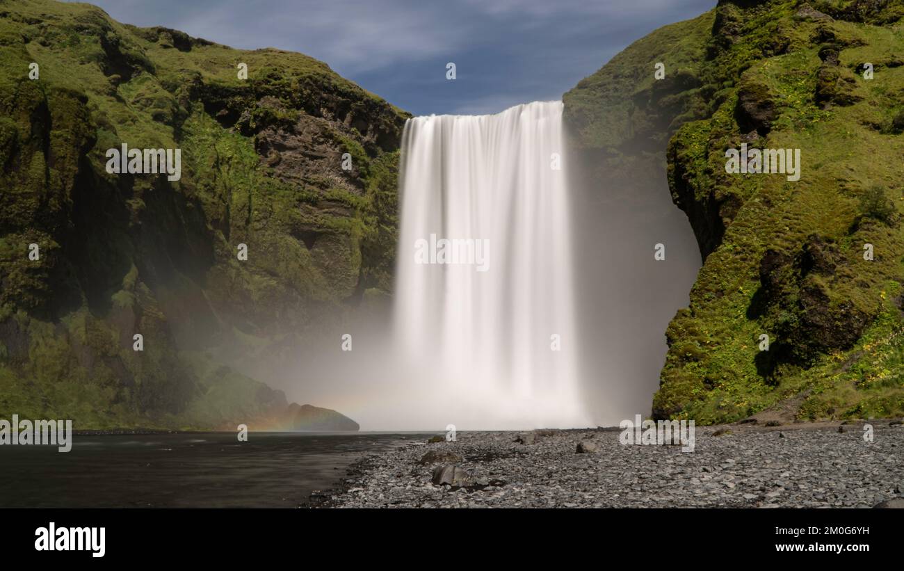 A beautiful shot of the flowing Skogafoss waterfall in the cliffs of ...