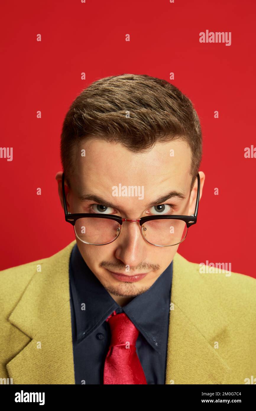 Portrait of young man in stylish jacket and glasses posing over red ...