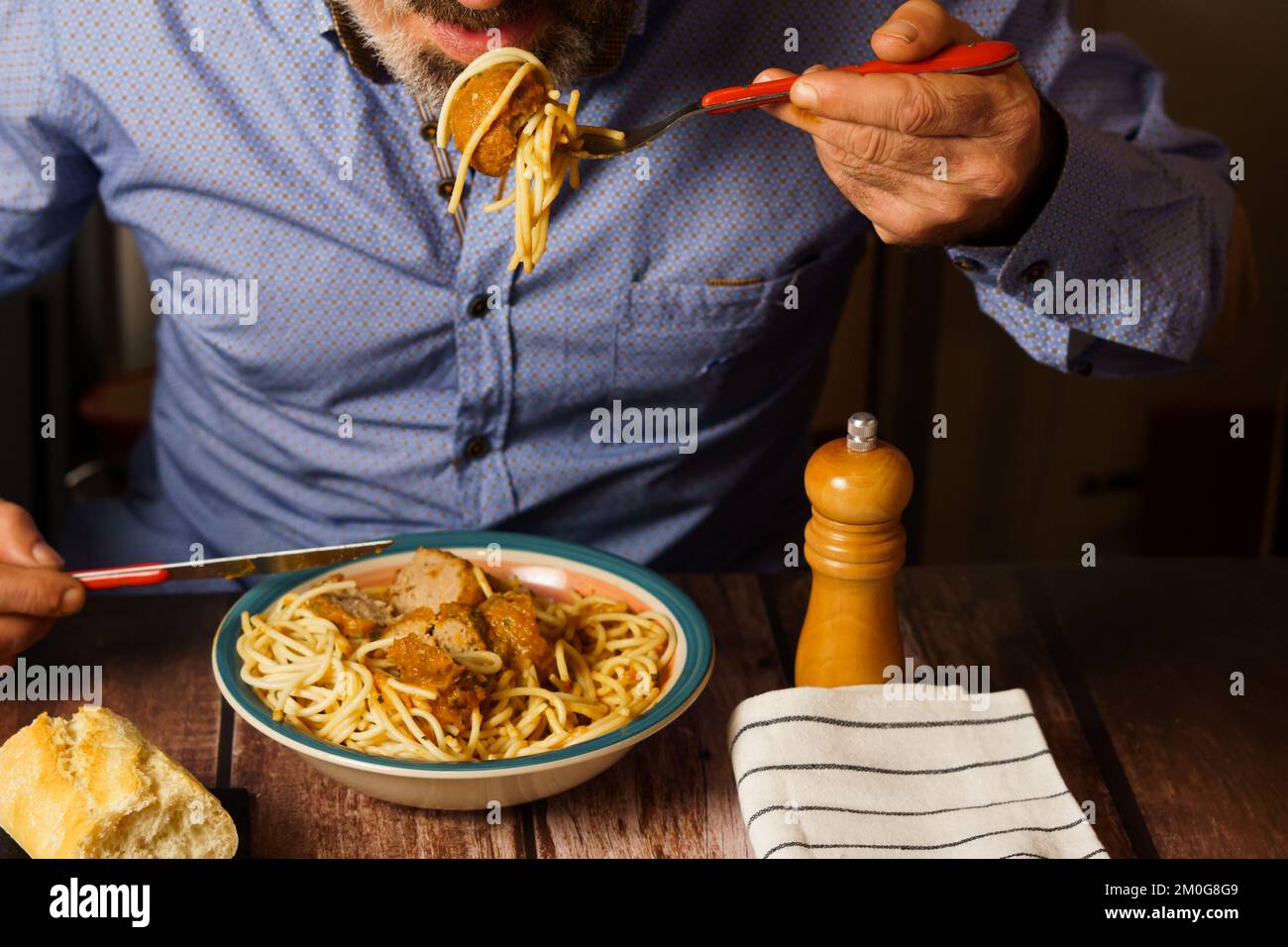 man with beard and blue shirt eating meatballs with spaghetti in a ...