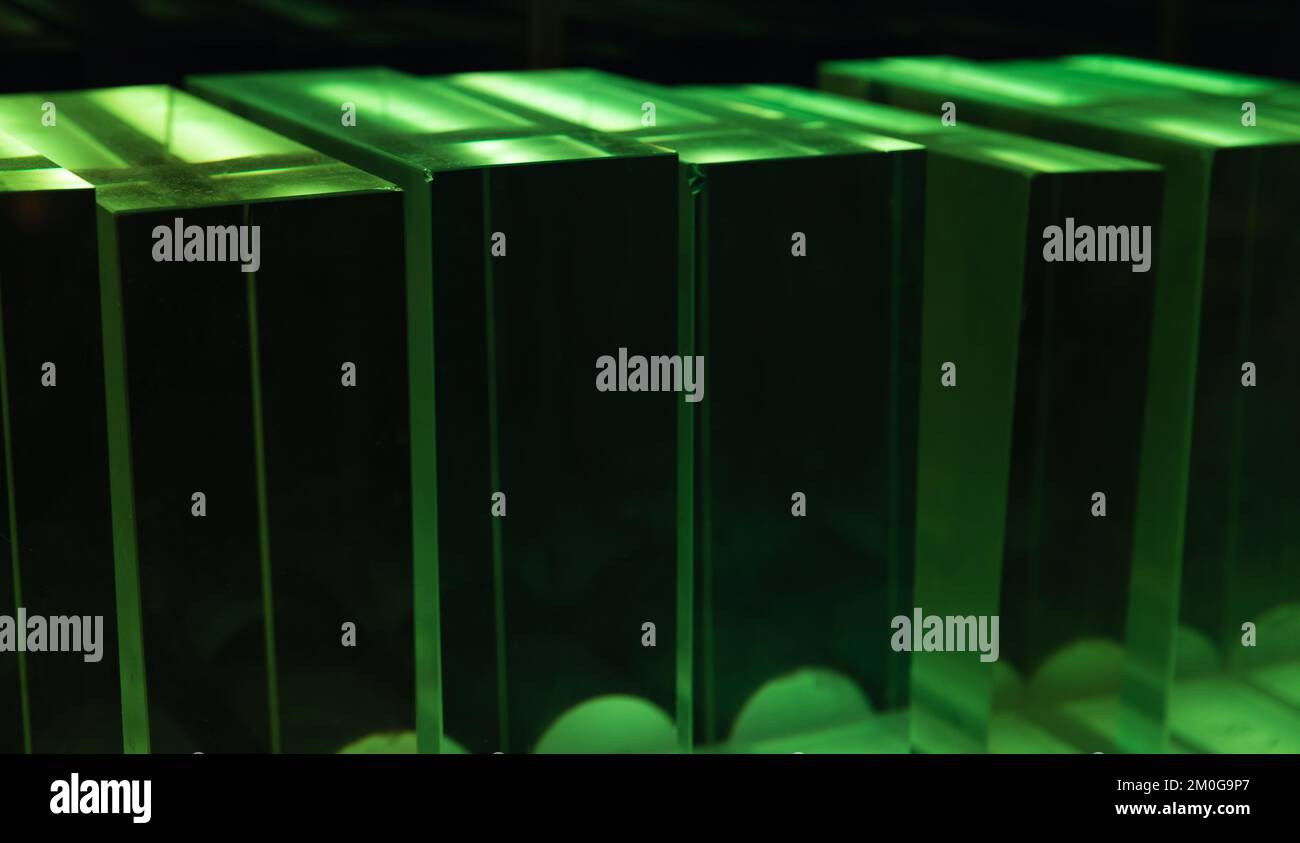 Solid glass blocks stand in a row in a dark room with green ...