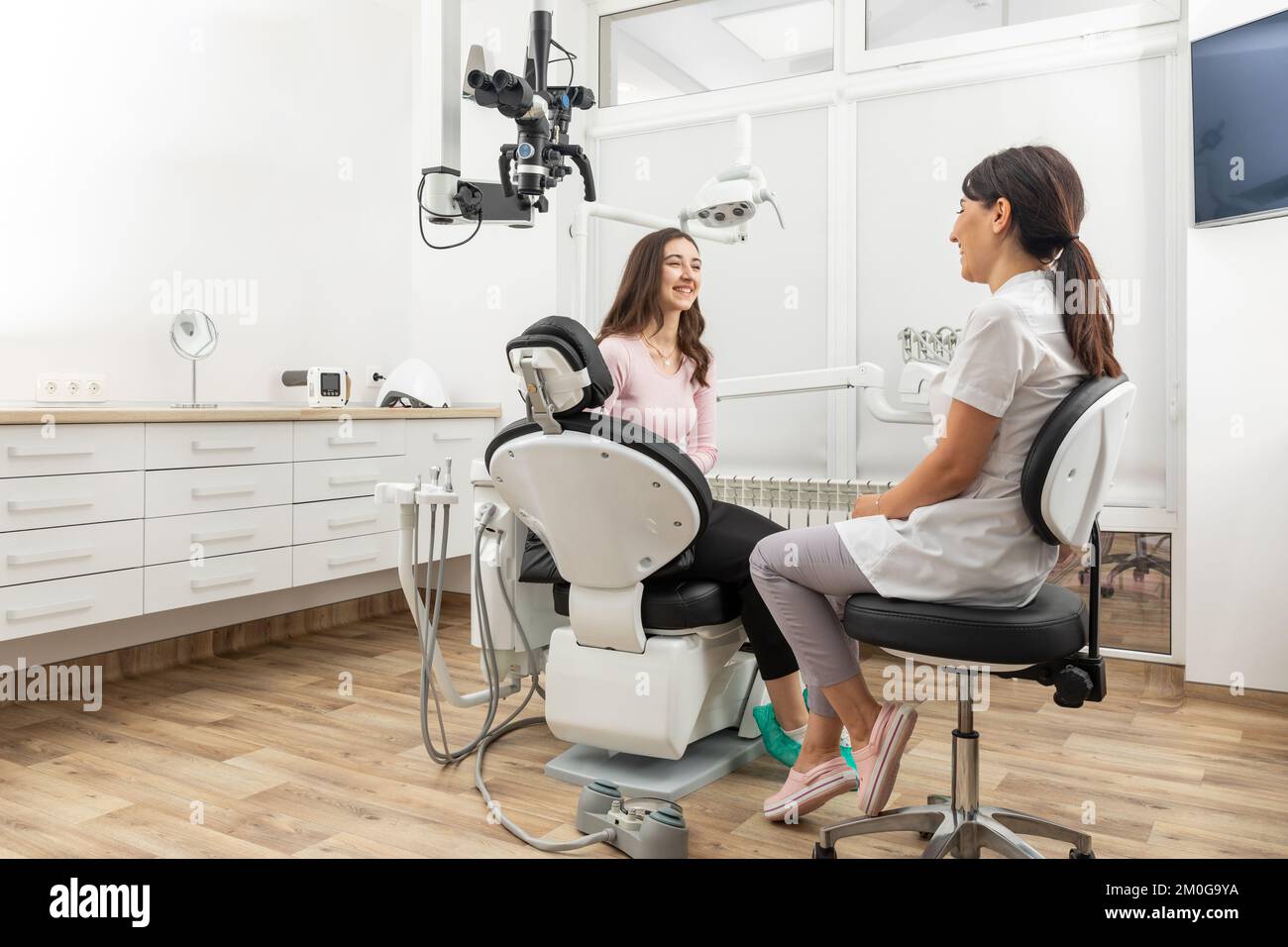 Female dentist talking to a young patient during appointment in modern ...
