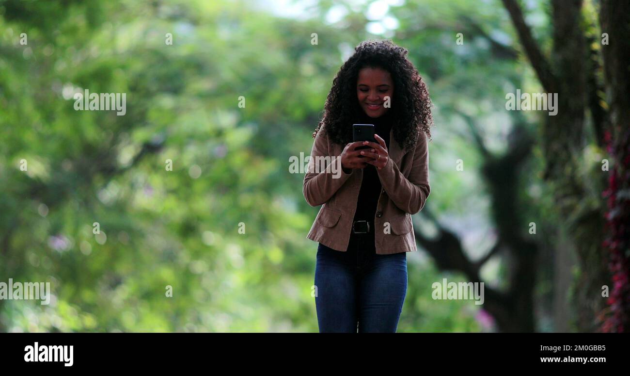 African woman using cellphone while walking outside. Person staring at ...