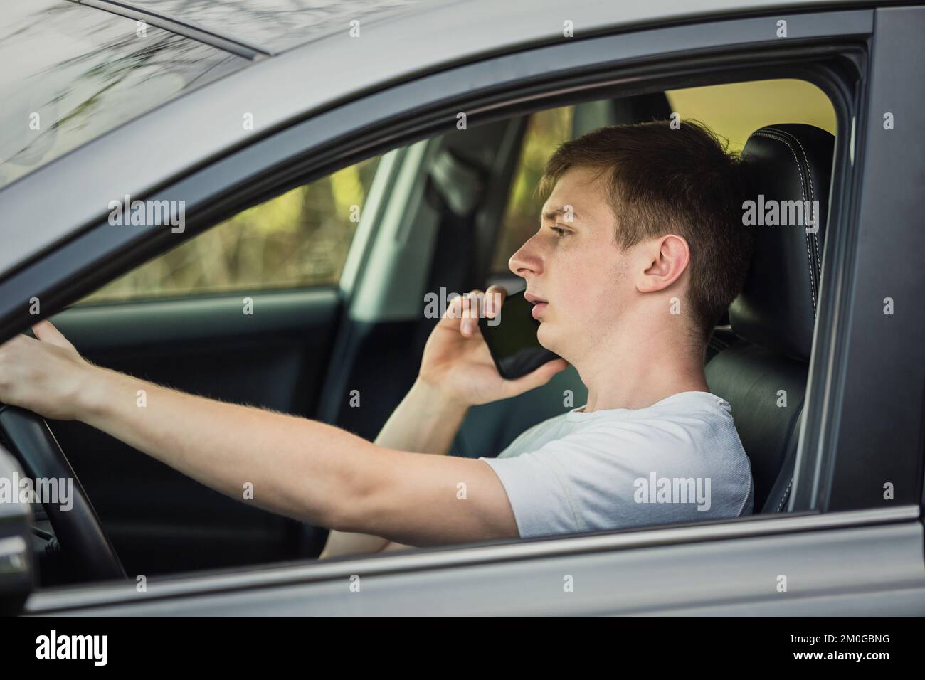 Young man unsafe driving while phone talking in front of the steering ...