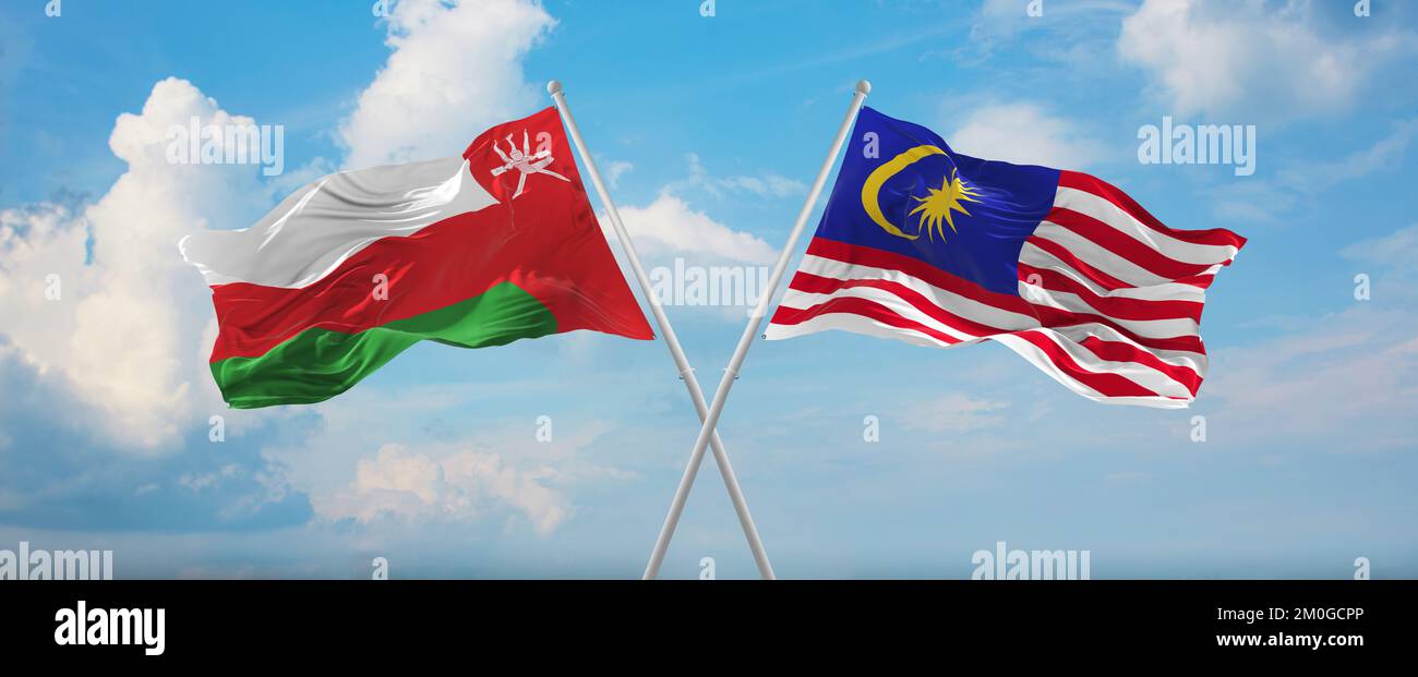 two crossed flags Malaysia and Oman waving in wind at cloudy sky ...