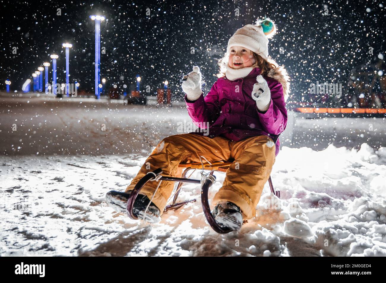 A little girl is sledding on a snowy winter evening. Falling realistic ...