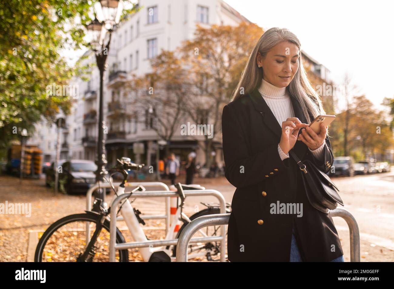 Long-haired mid aged woman with a phone in hand standing near the bikes ...