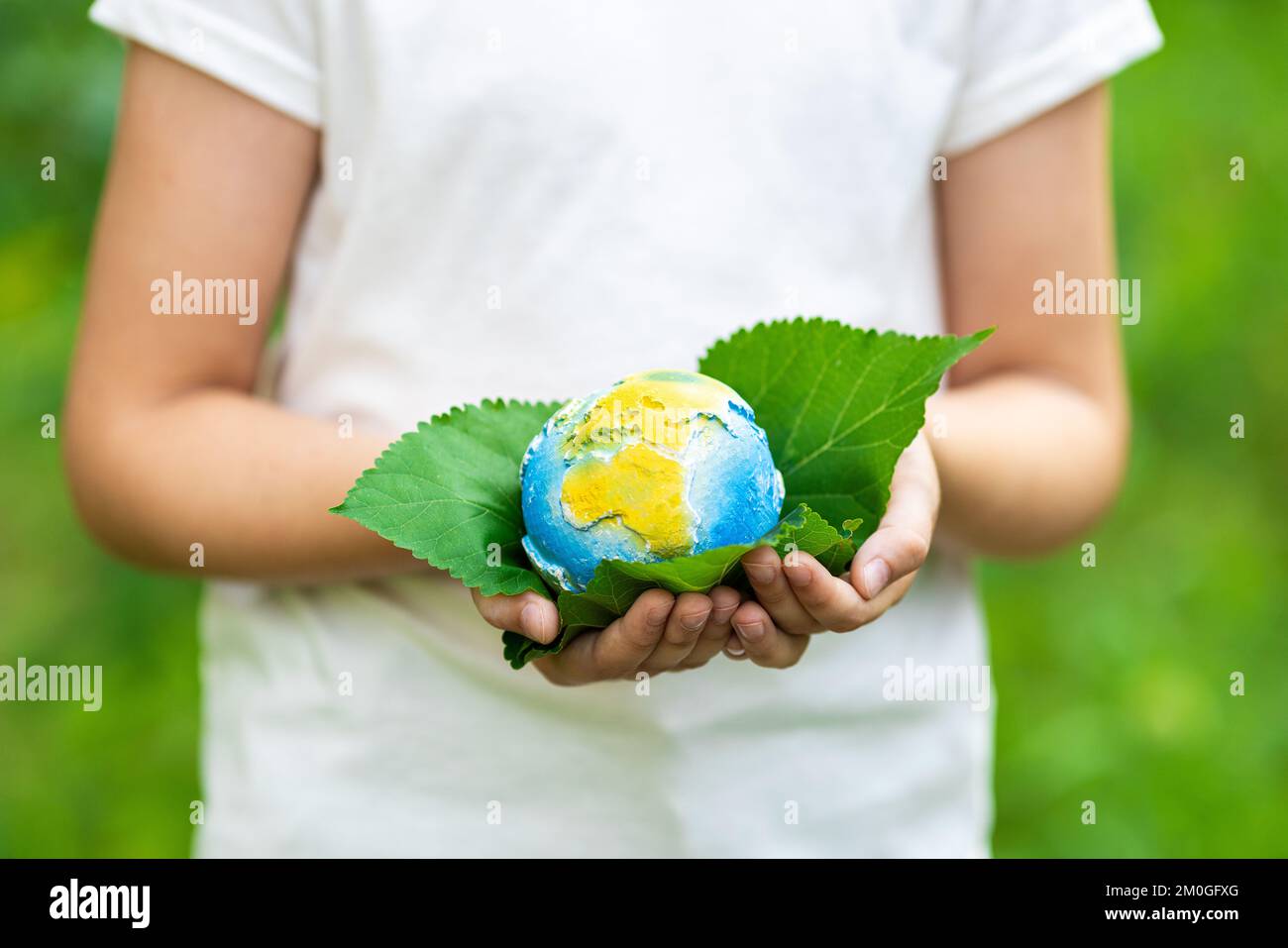 Kid holding small planet in hands against spring or summer green ...