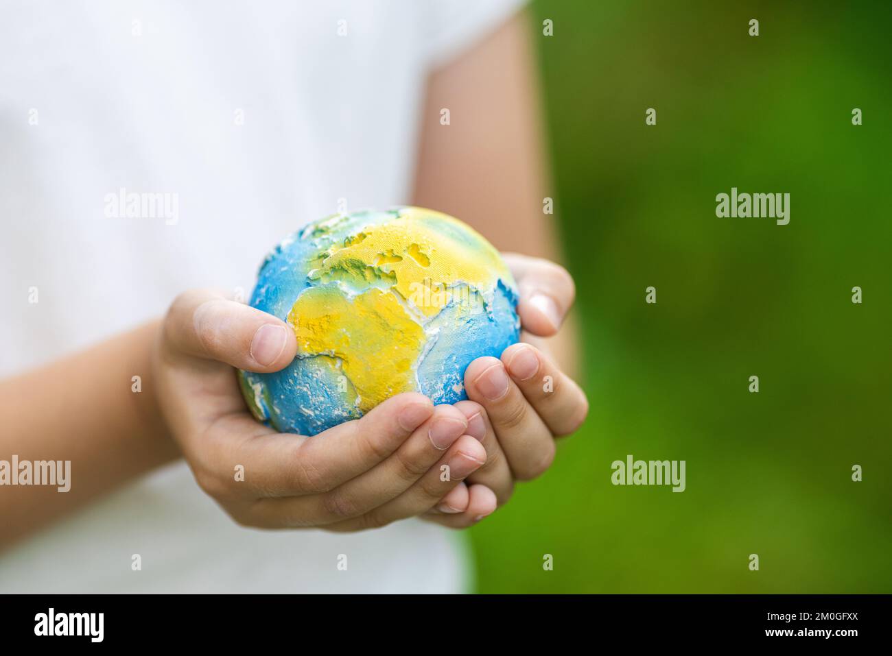 Kid holding small planet in hands against spring or summer green ...