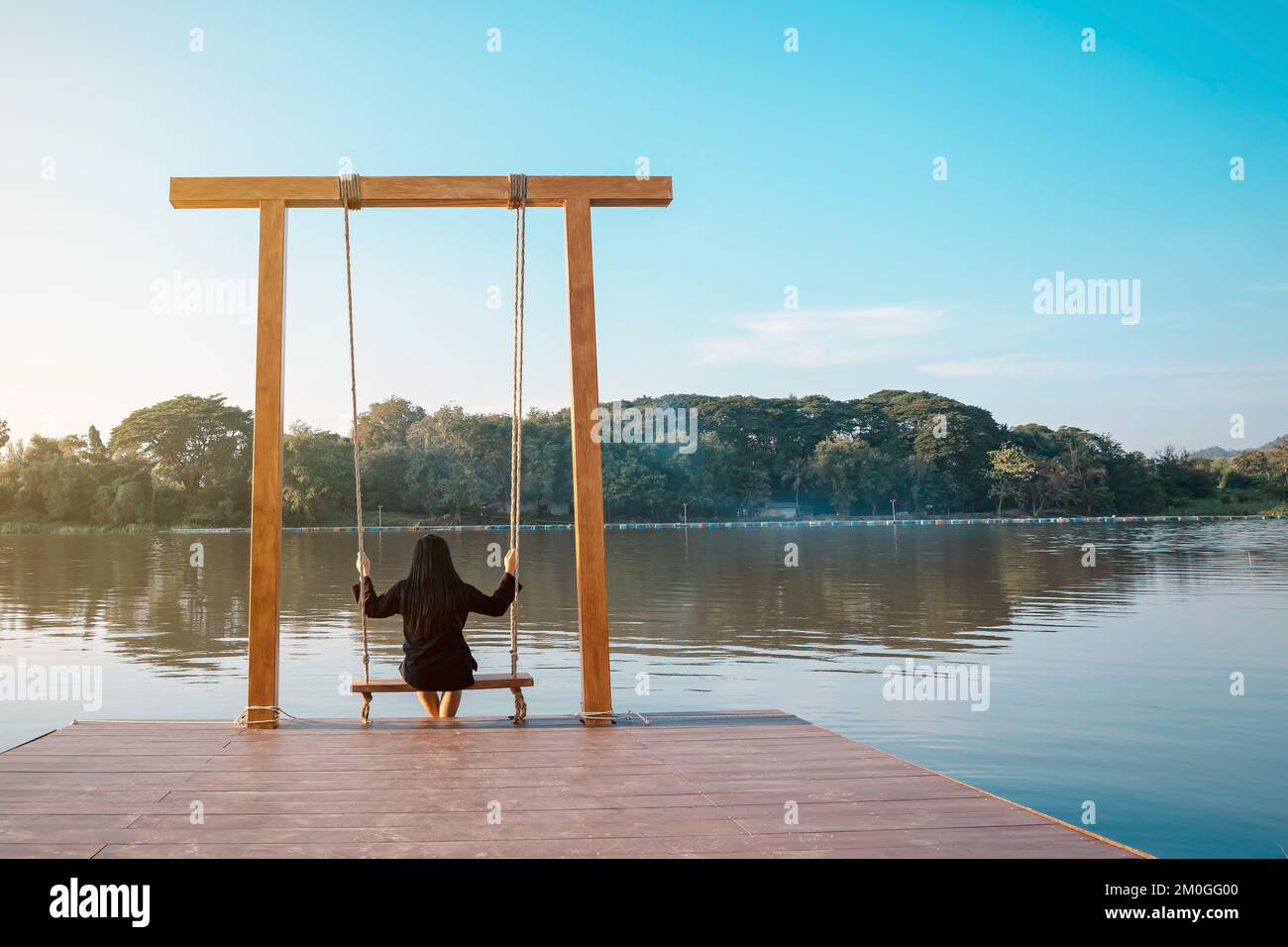 Back view of young Asian woman sits relax and playing on wooden bench ...