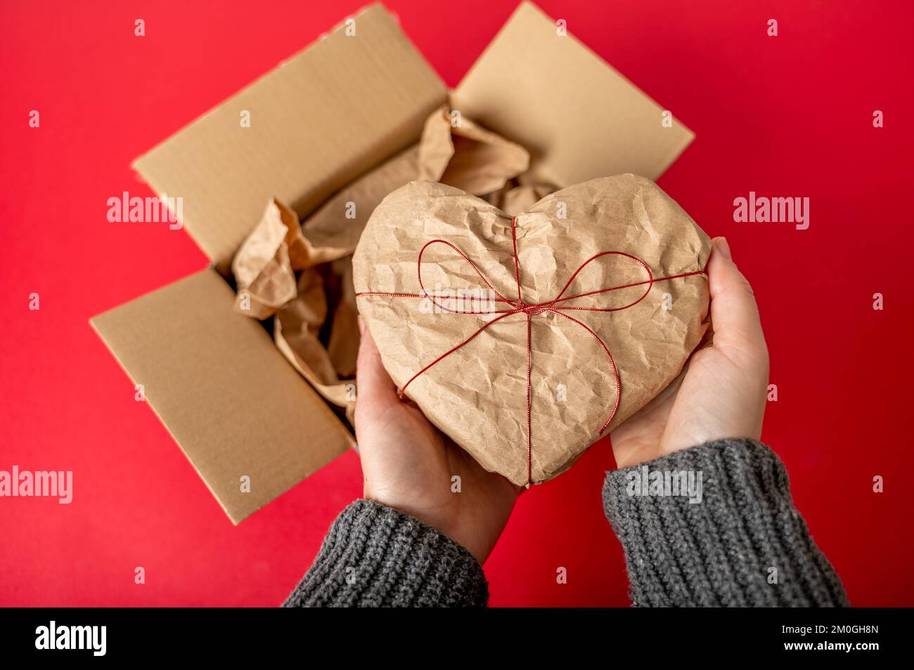 Hands holding Heart-shaped gift box wrapped in kraft paper on red ...