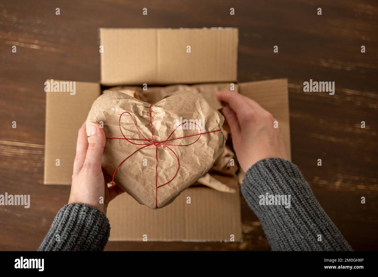 Hands holding Heart-shaped gift box wrapped in kraft paper on wooden background. Just unpacked ...