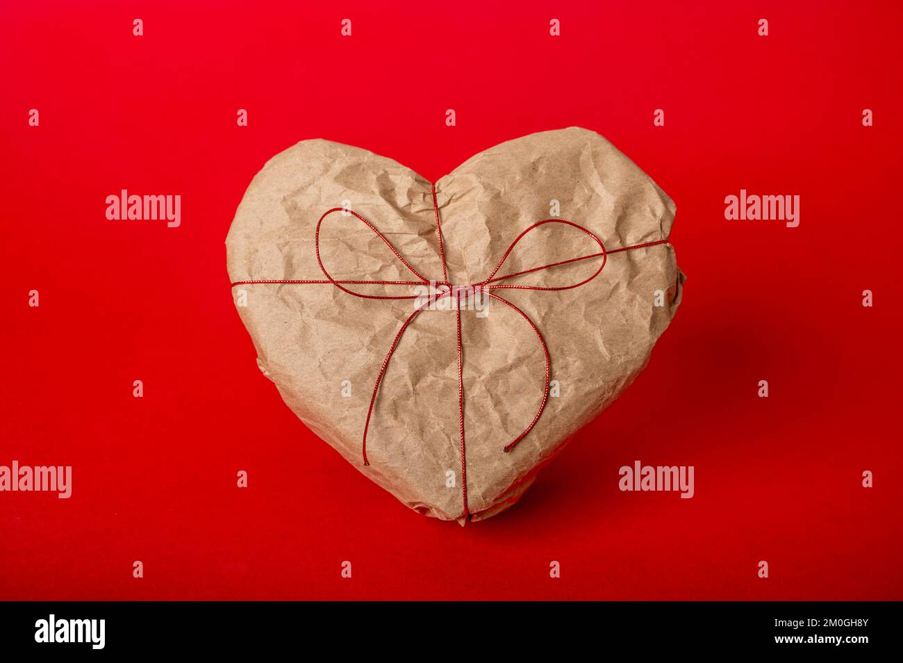 Heart-shaped gift box wrapped in kraft paper on red background Stock ...