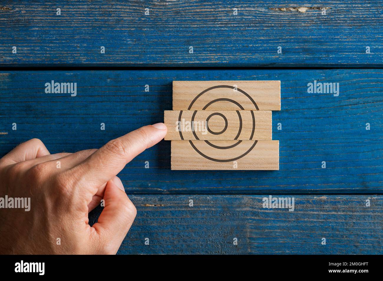 Male hand stacking three wooden pegs with a target sign on them in a ...