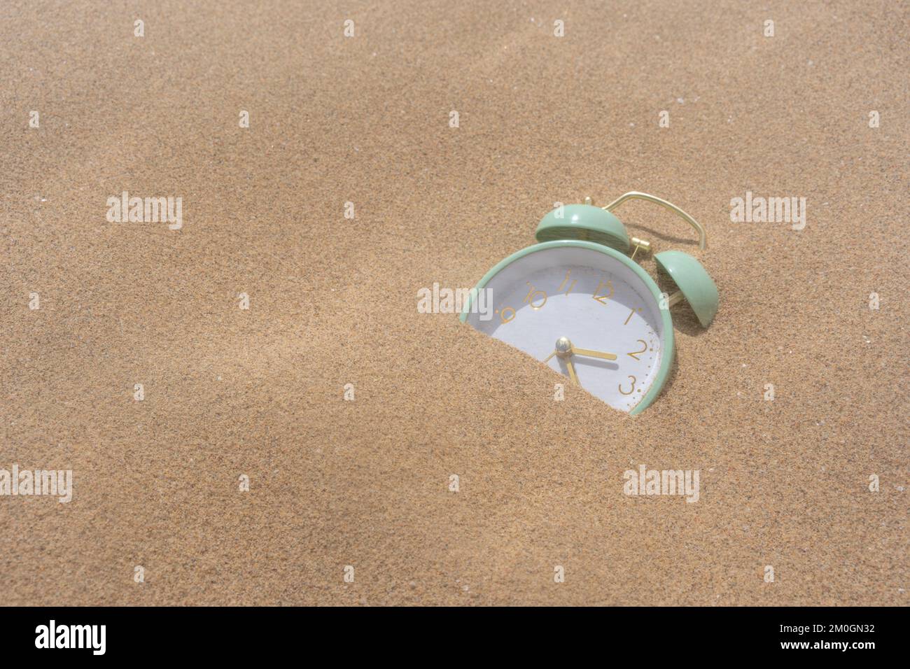 A closeup of a green alarm clock half covered under sand grains Stock ...