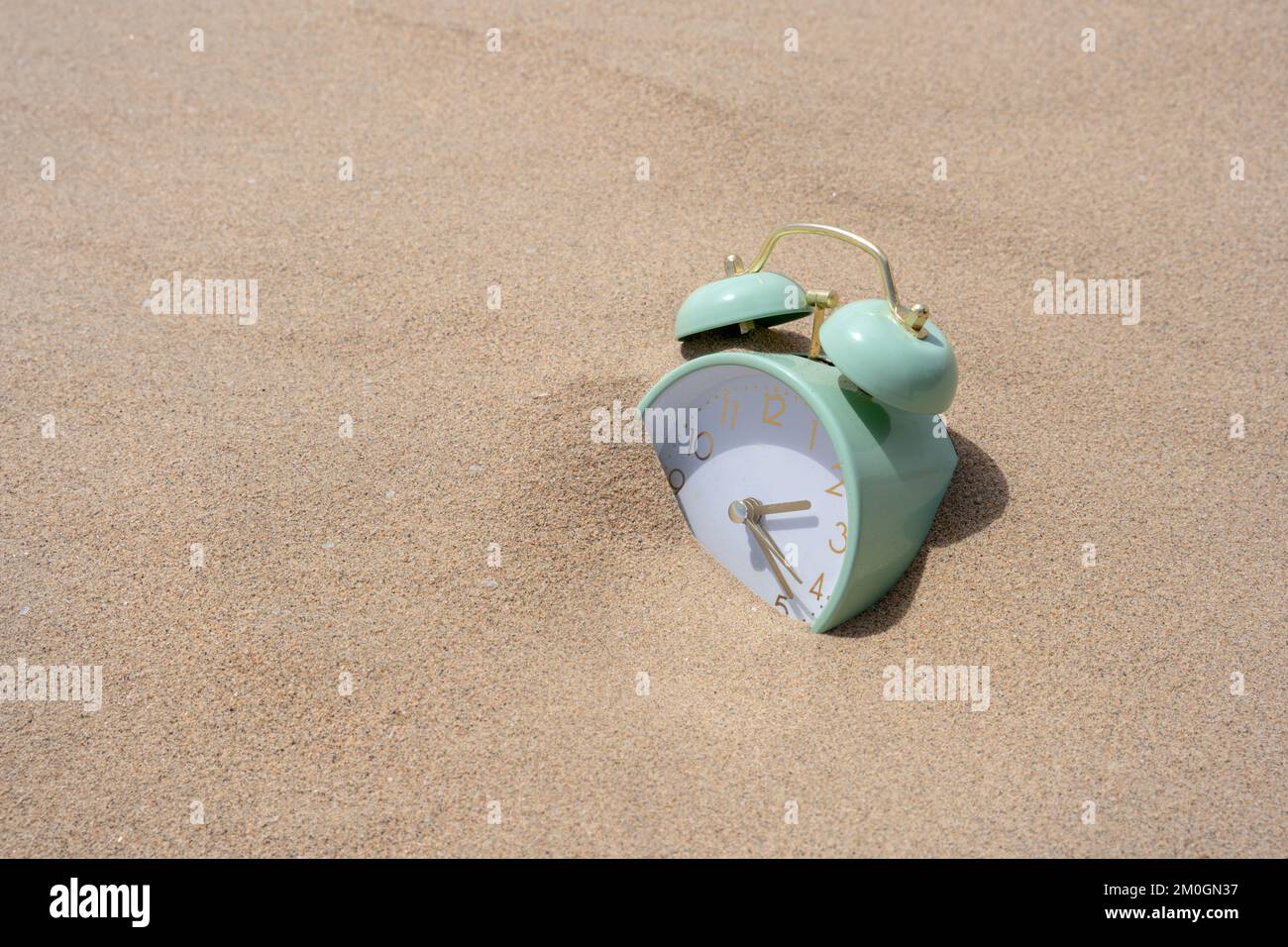 A closeup of a green alarm clock half covered under sand grains Stock ...