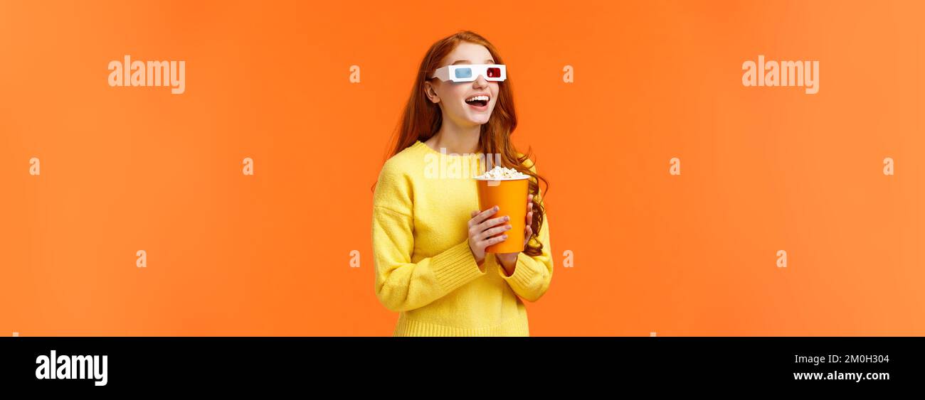 Girl eating popcorn, smiling amused as staring at large screen watching ...