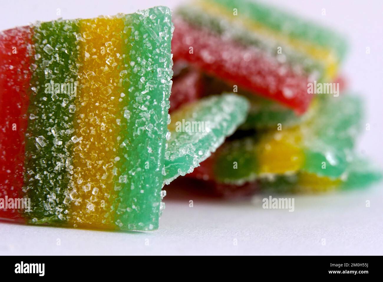 Rainbow stripes of sour jelly candies in sugar sprinkles on a white ...