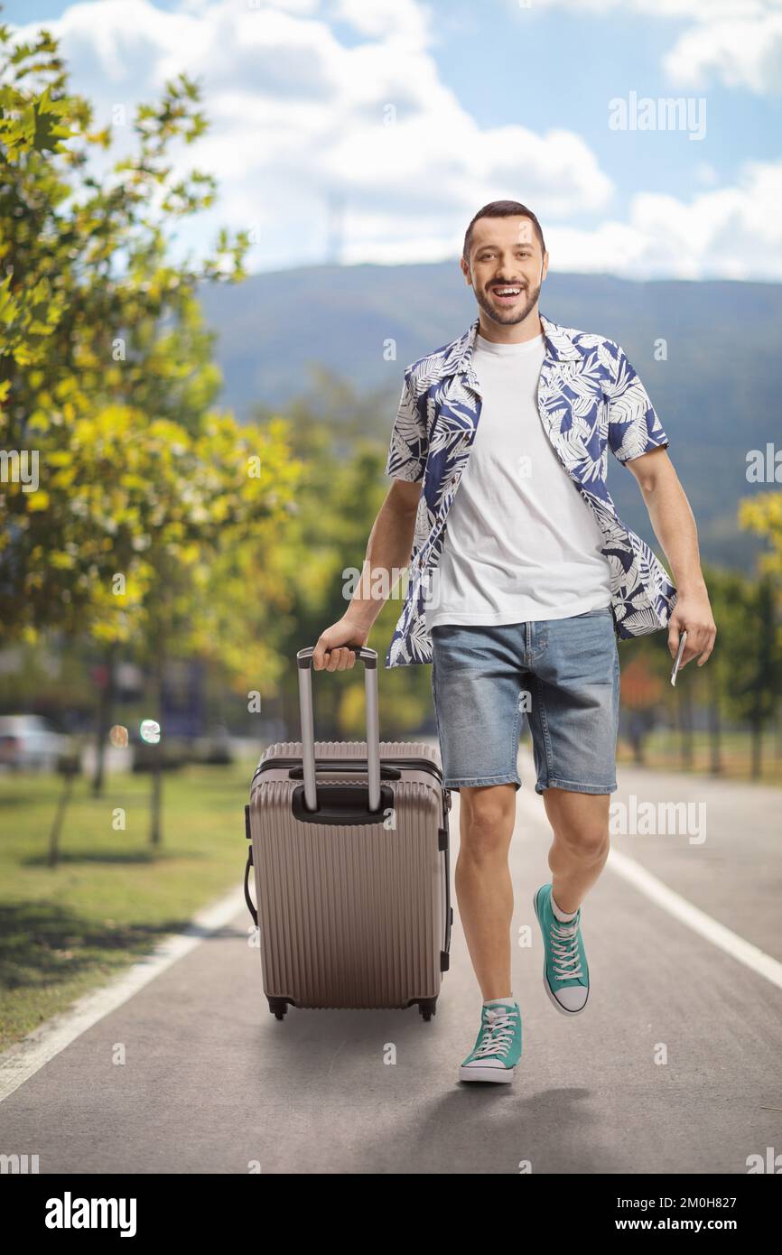 Full length portrait of a smiling man walking and pulling a suitcase in ...