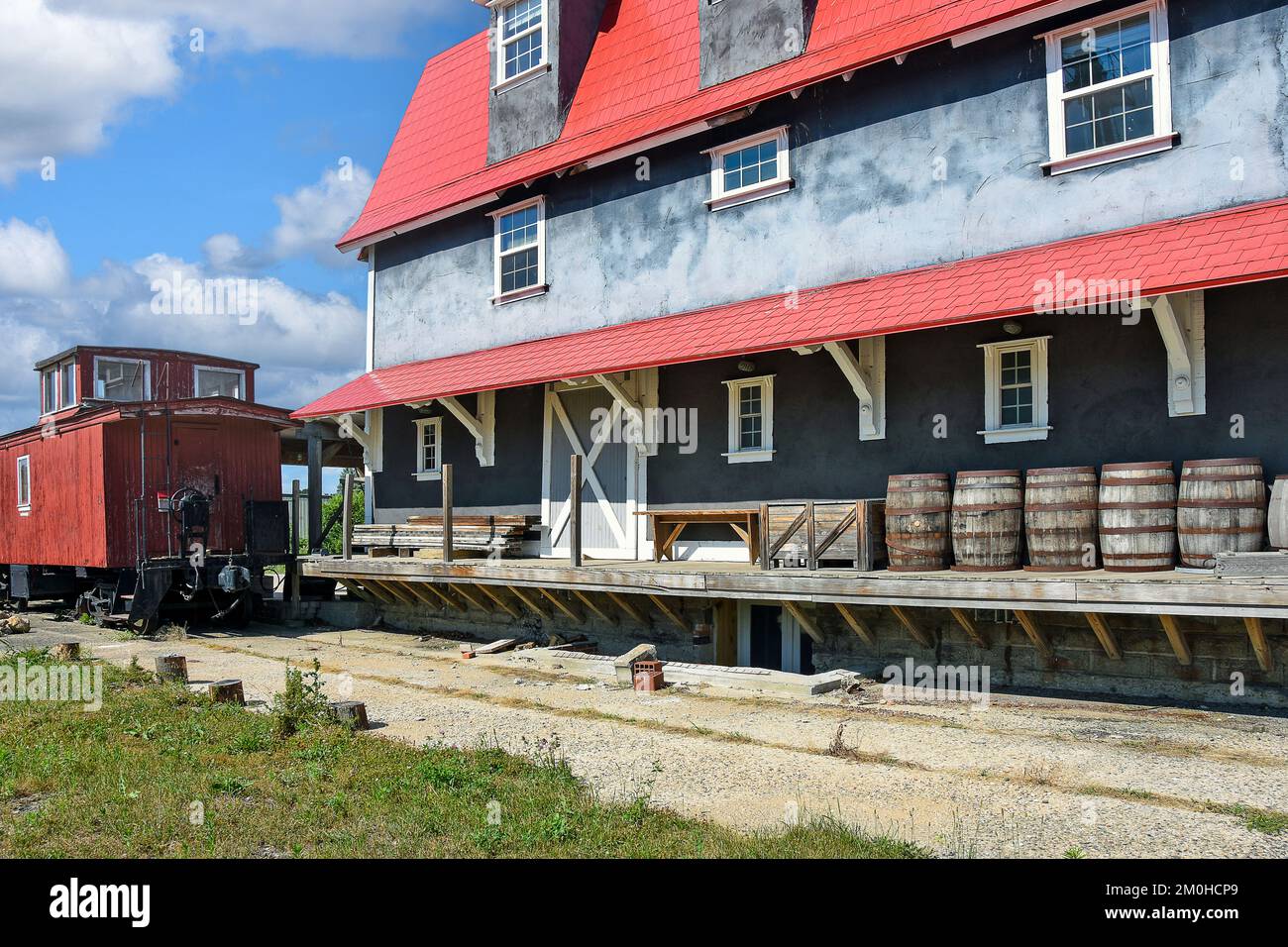 A row of old wooden barrels on a train station dock with a red caboose ...