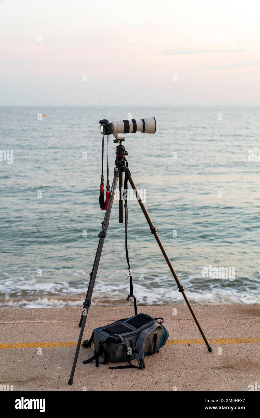 Camera on tripod on the seawall against the sea and sky. Camera bag ...