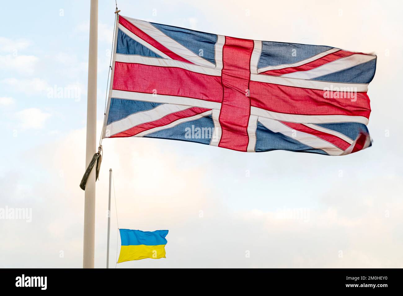 Union Jack and Ukrainian flag flying at half mast against a dull pale ...