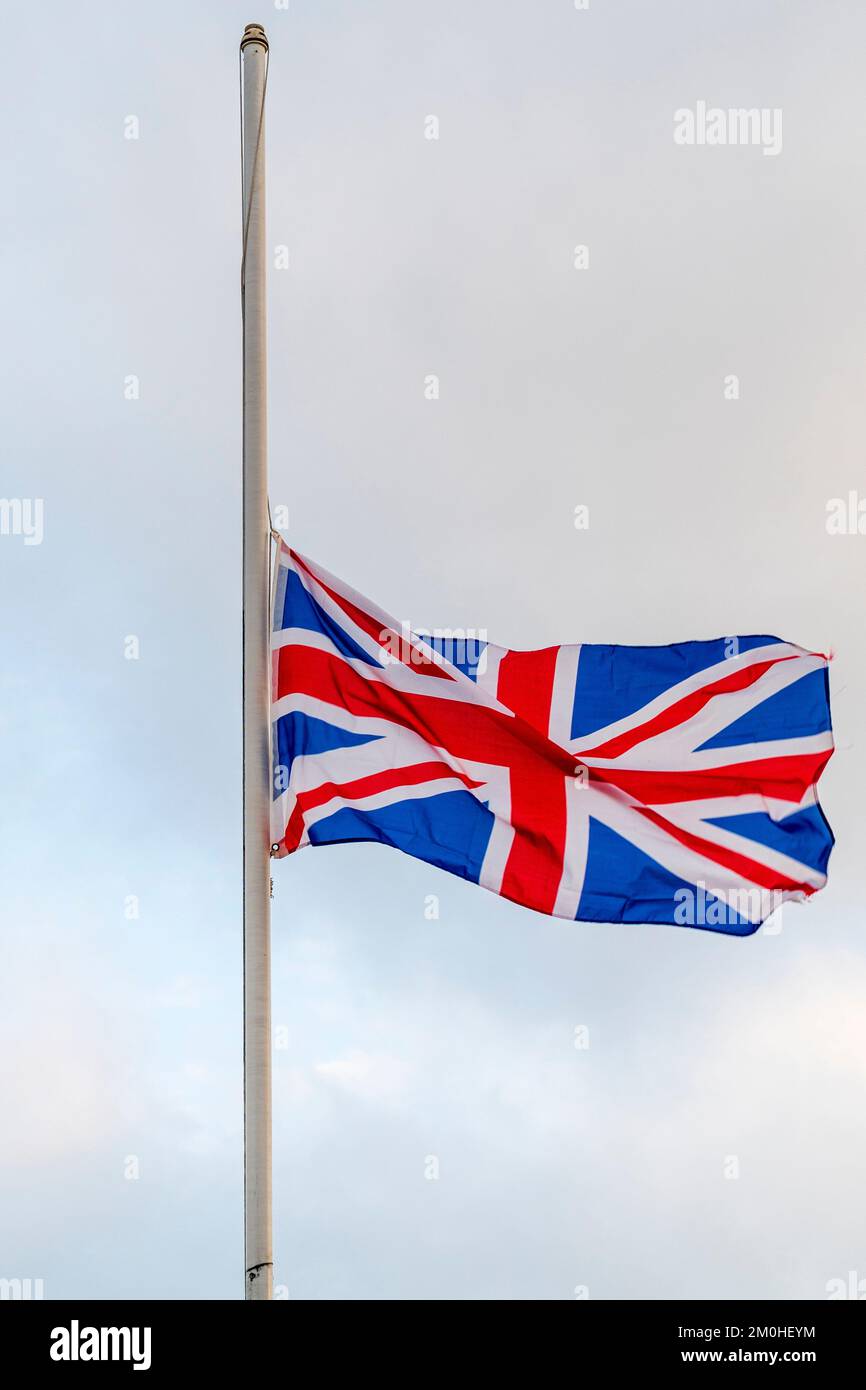 Union Jack flag flying at half mast against a dull pale blue and white ...