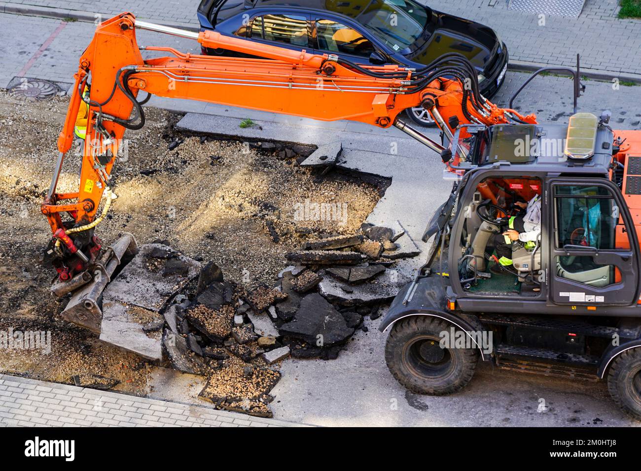 An excavator breaks up the old asphalt layer with a bucket during ...