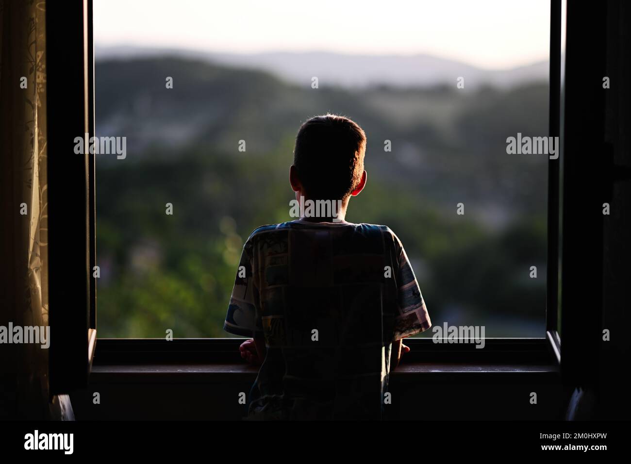 Back of boy looking from window in sunset Stock Photo - Alamy