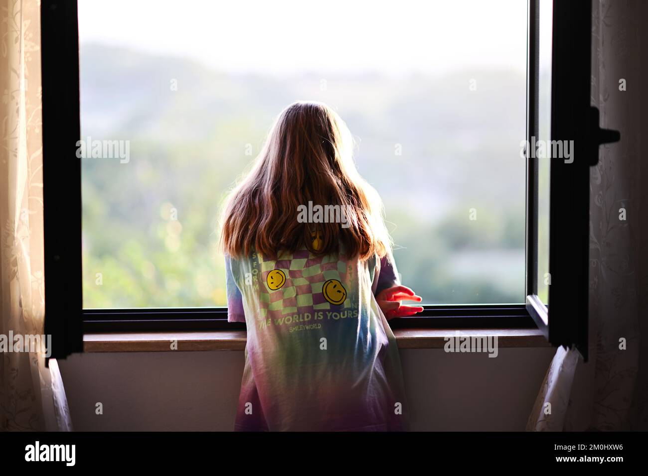 Back of girl looking from window in sunset Stock Photo - Alamy