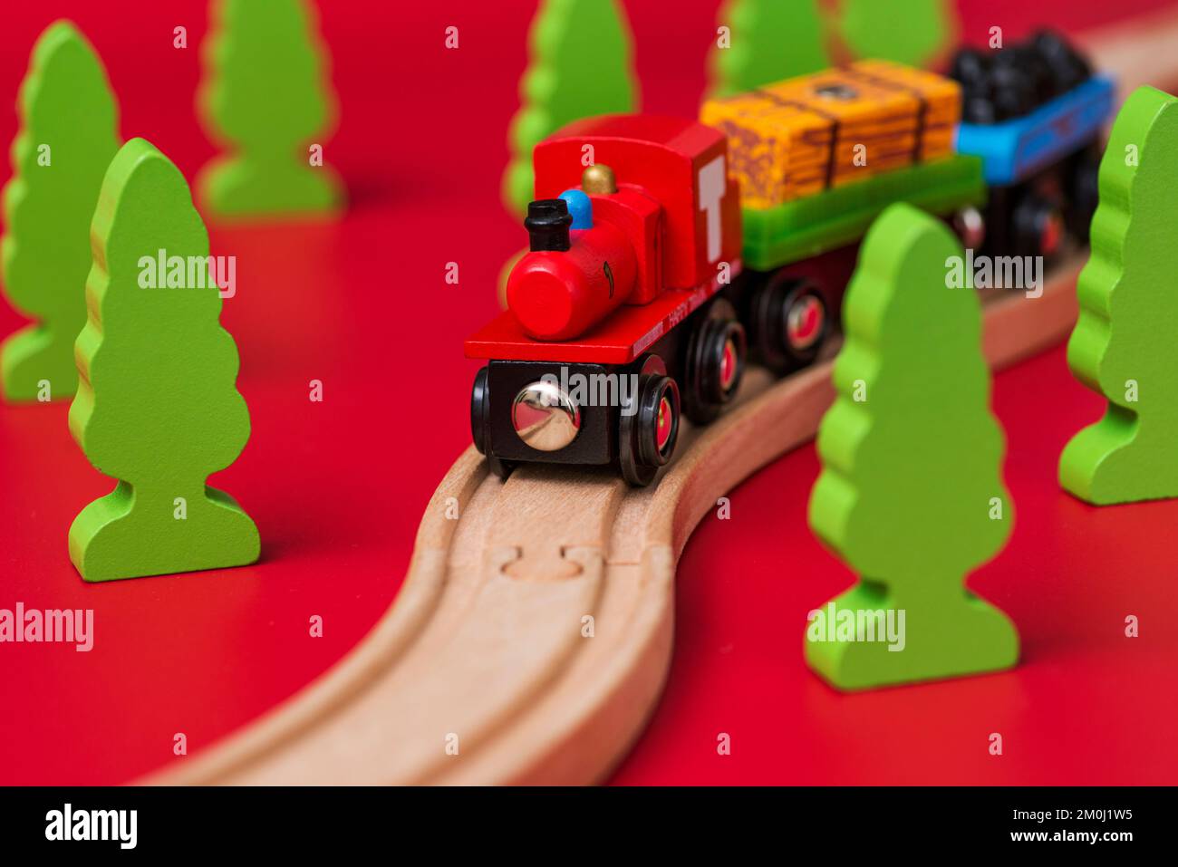 Wooden toy train on the railroad among green trees on red background ...