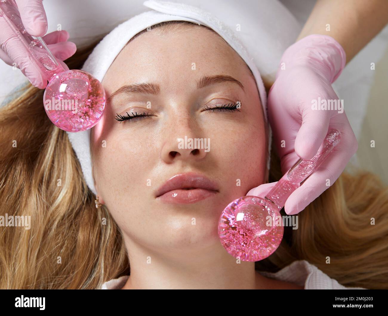 Young woman receiving facial massage with glass balls in beauty salon ...
