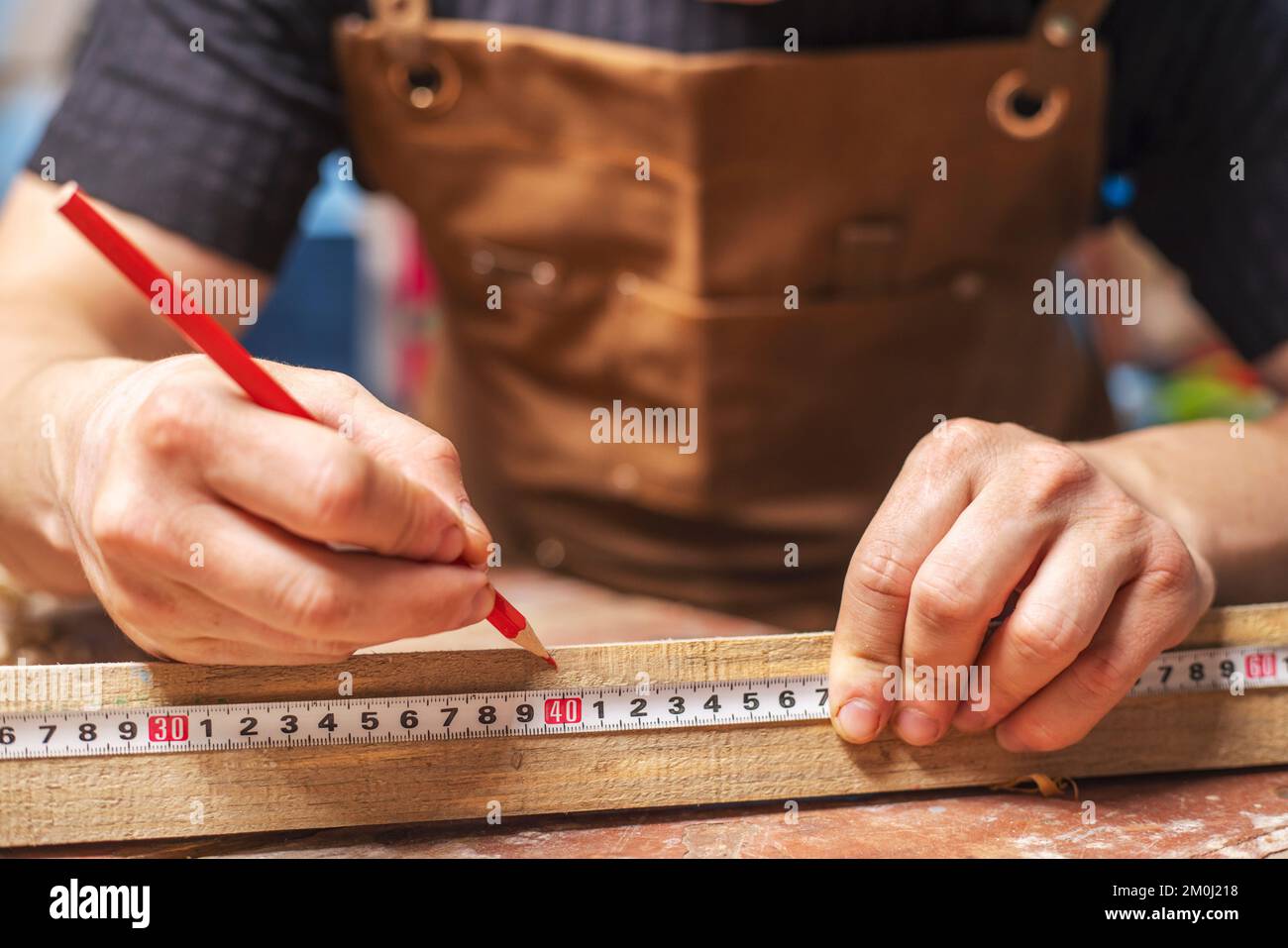 A carpenter making a mark with red pencil after measuring a wooden ...