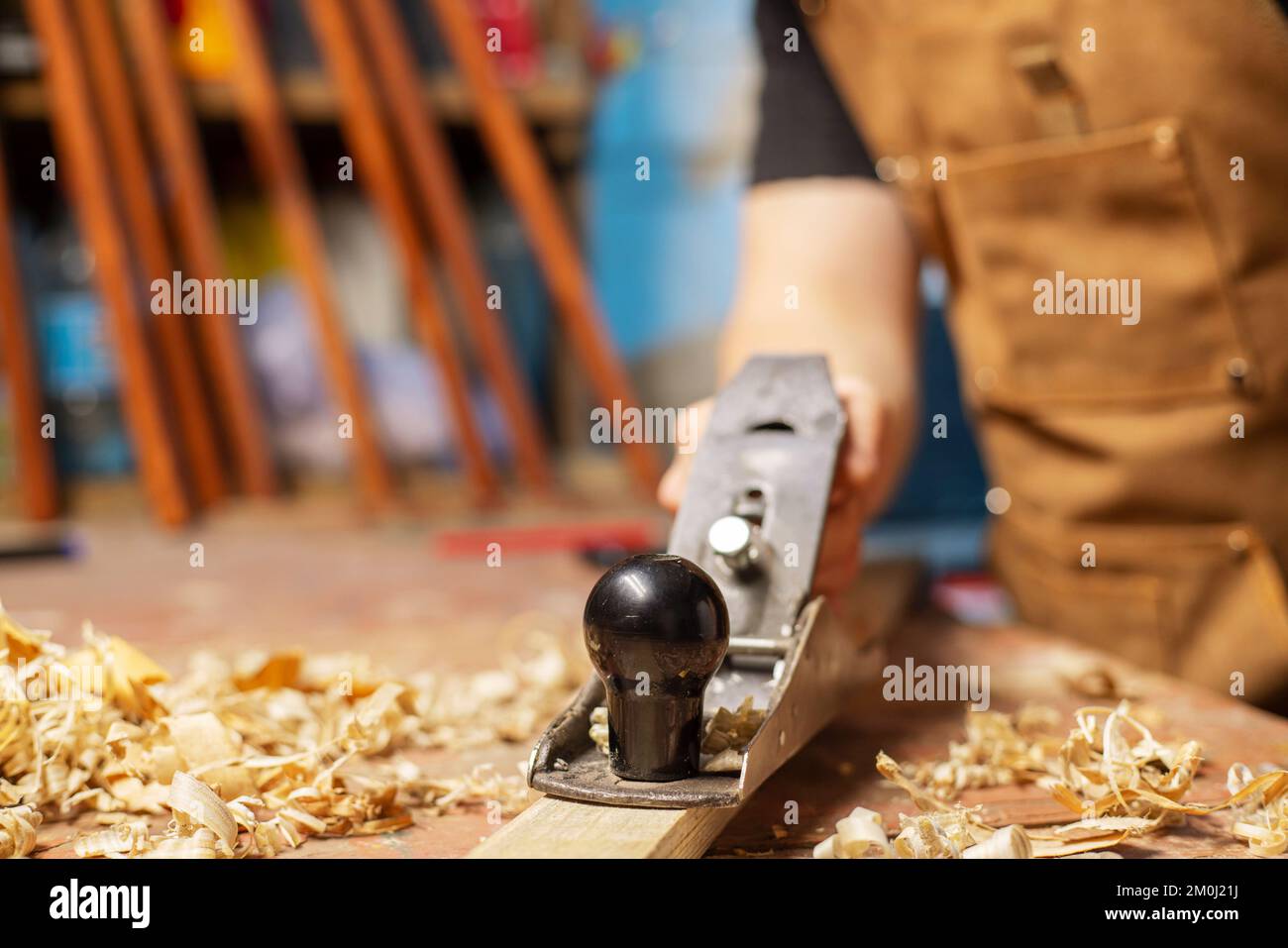 Carpenter in an apron planing a wooden board with a planer, workplace ...