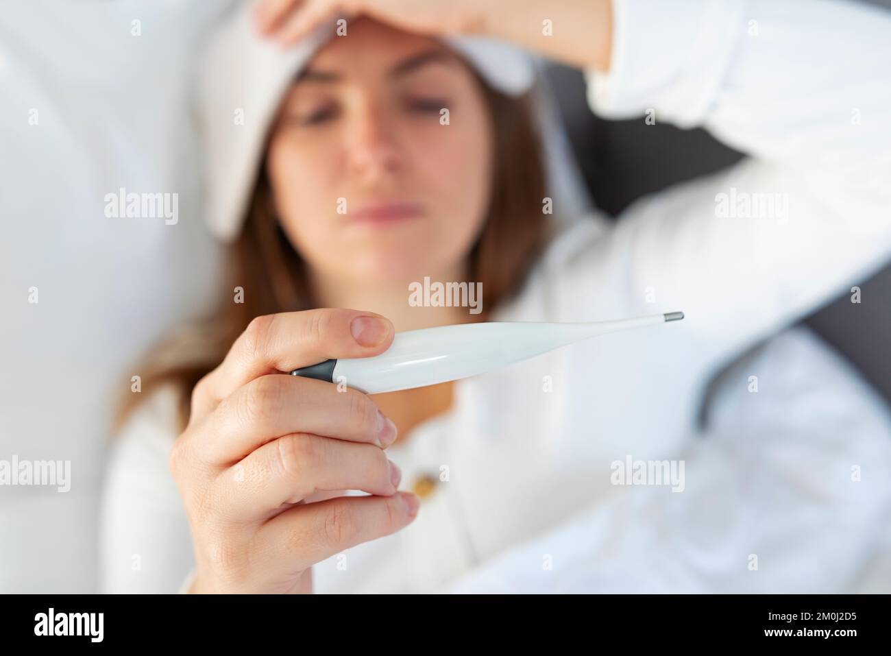 Woman with flu lying in bed, she is measuring her temperature ...