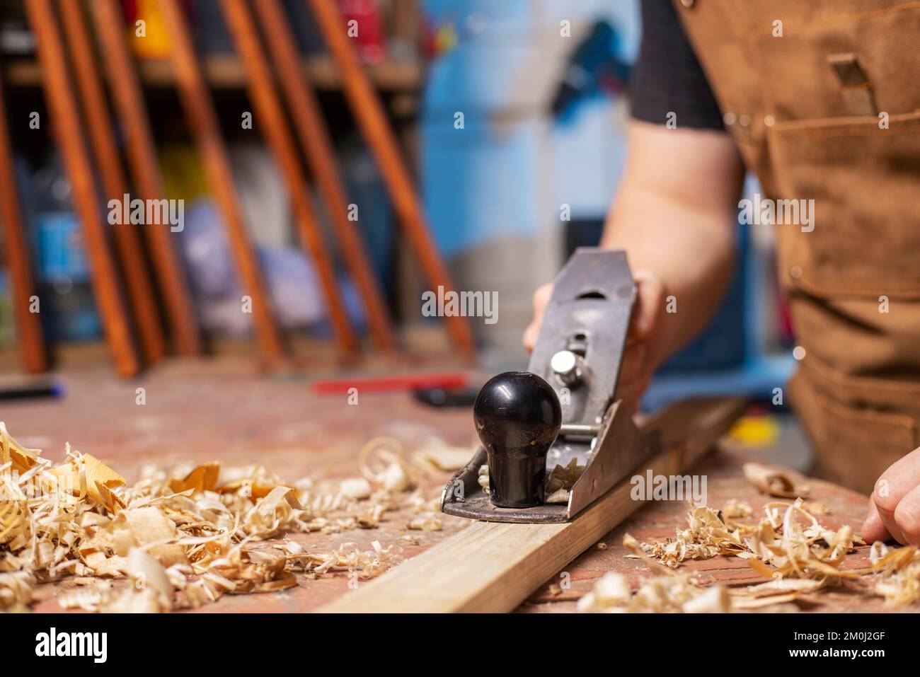 Carpenter in an apron planing a wooden board with a planer, workplace ...