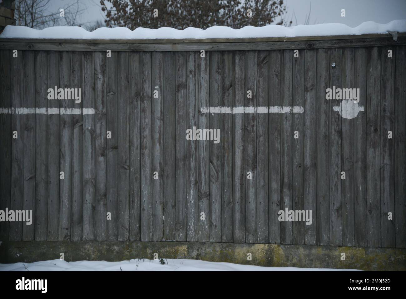 gray wooden fence on a concrete foundation is covered with white snow ...