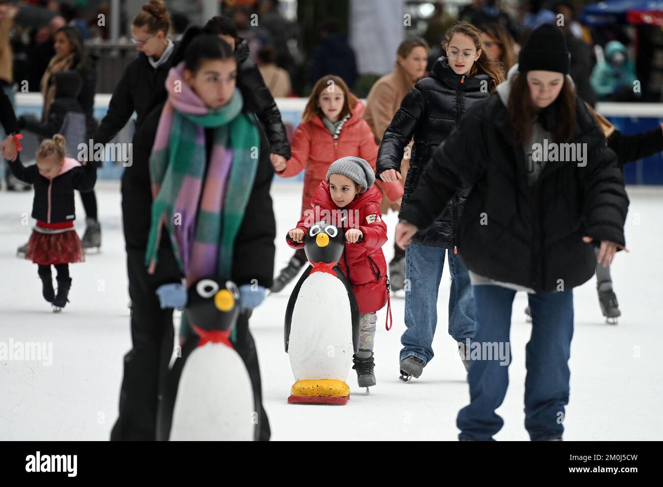 A child learning how to ice skate holds on to a penguin skating aid as ...
