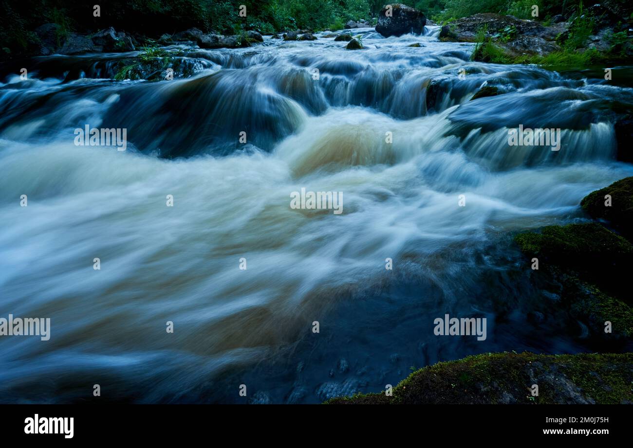 A foamy river flowing through big rocks in the forest, long exposure ...