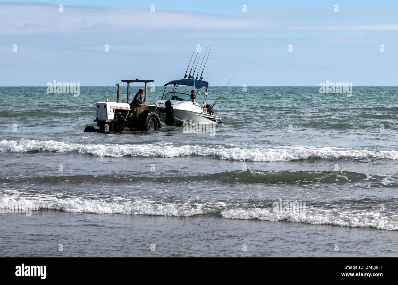 A tractor tows a small boat back onto land at Otaki Beach, Kapiti Coast ...