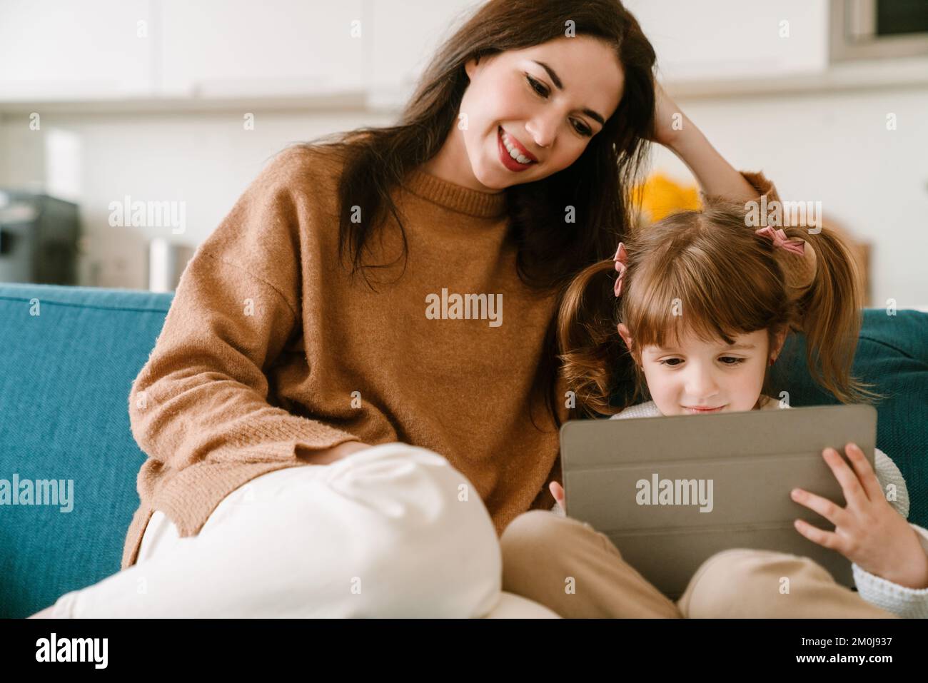 White girl using tablet computer while spending time with her mother at ...
