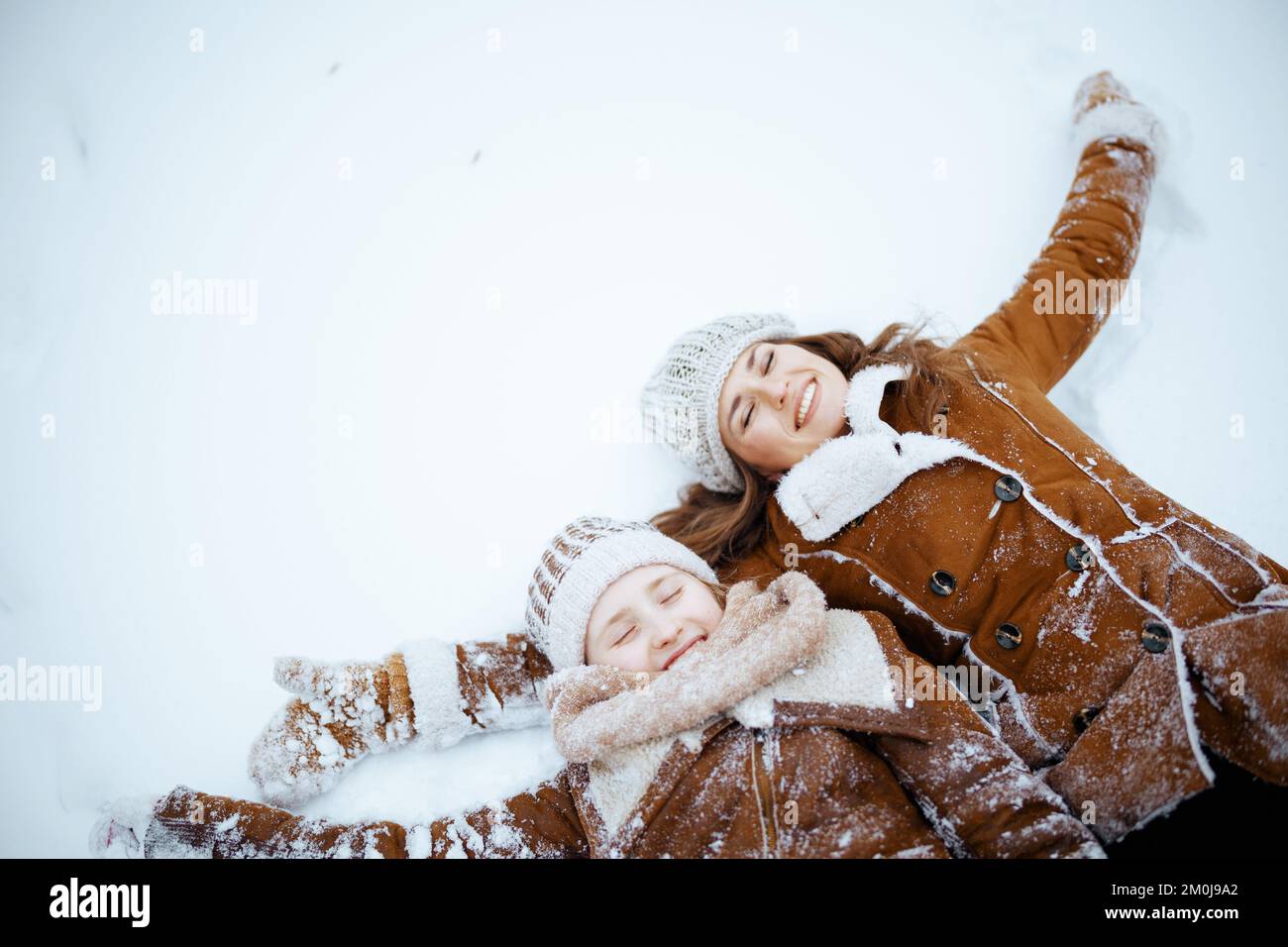 smiling modern mother and daughter in coat, hat, scarf and mittens ...
