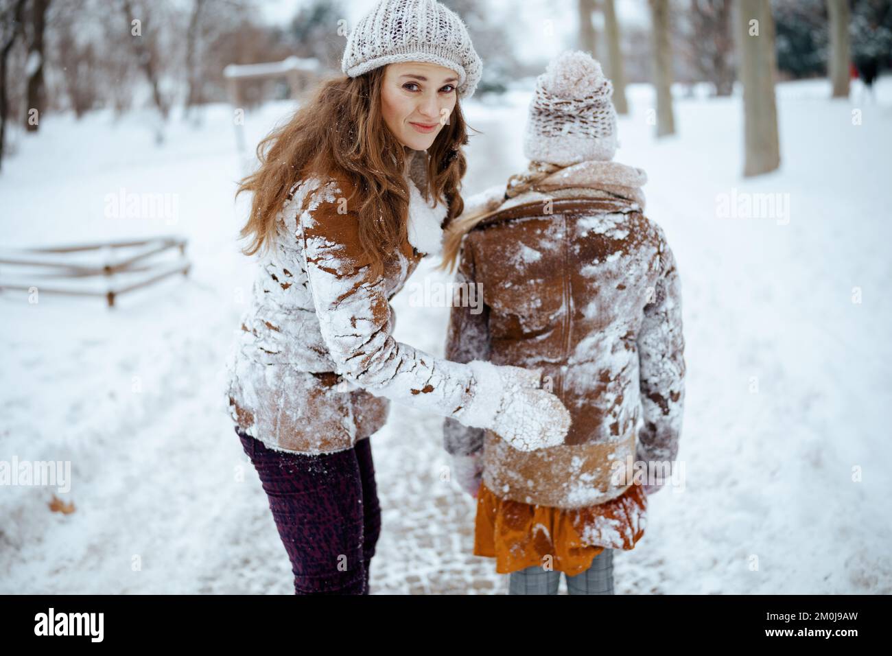 sad elegant mother and child in coat, hat, scarf and mittens shaking ...