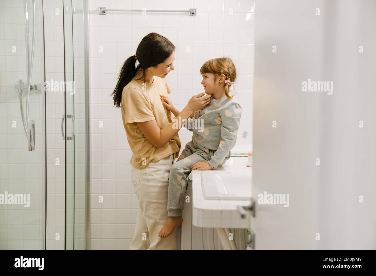 White woman smiling while talking with her daughter in bathroom at home ...