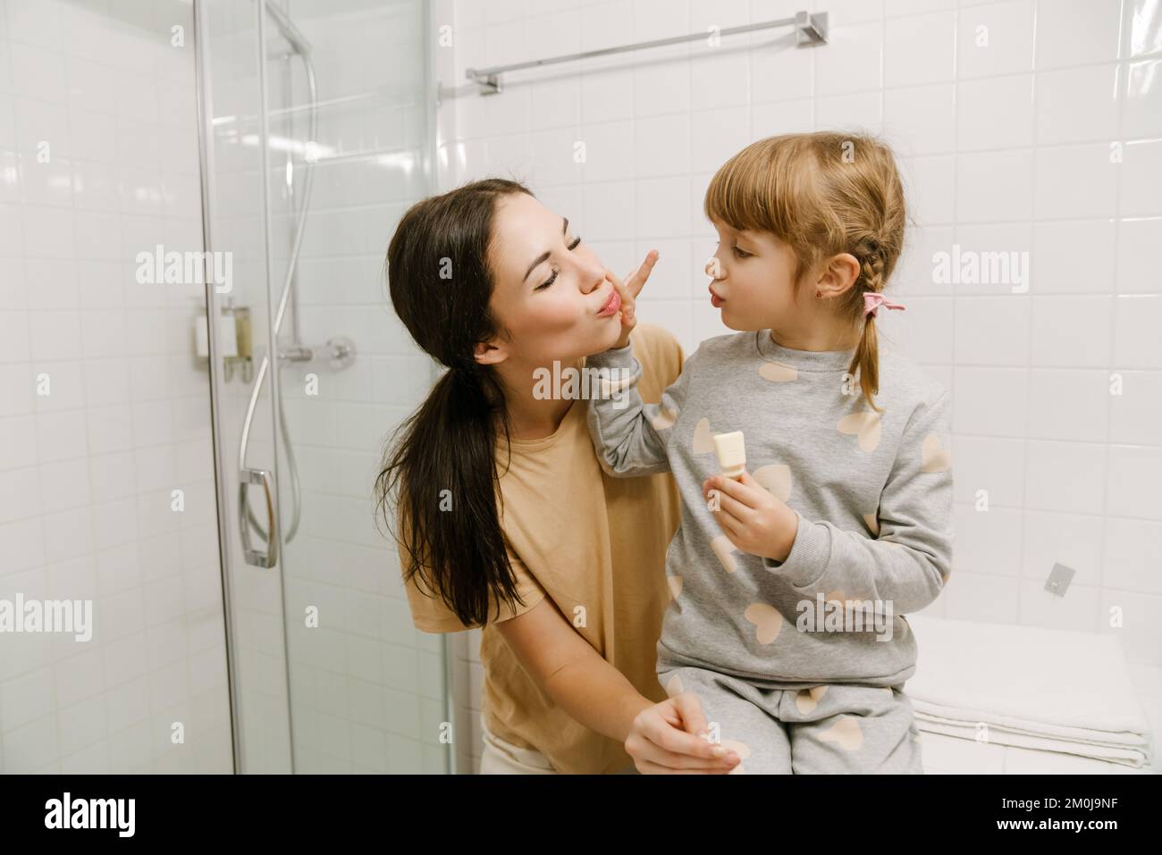 White woman smiling while doing makeup together in bathroom at home ...